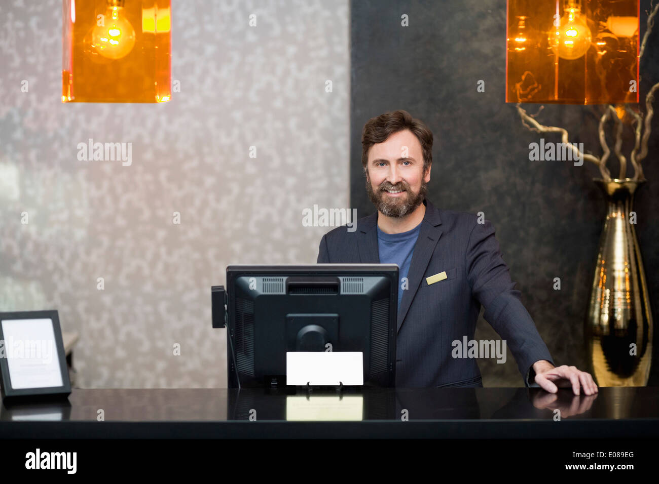 Portrait of confident male receptionist standing at counter in hotel ...