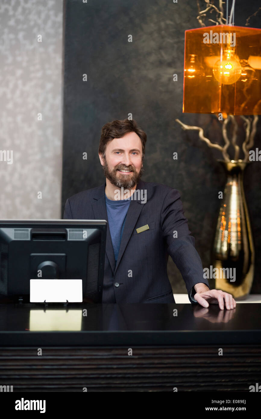 Portrait of smiling male receptionist standing at counter in hotel ...