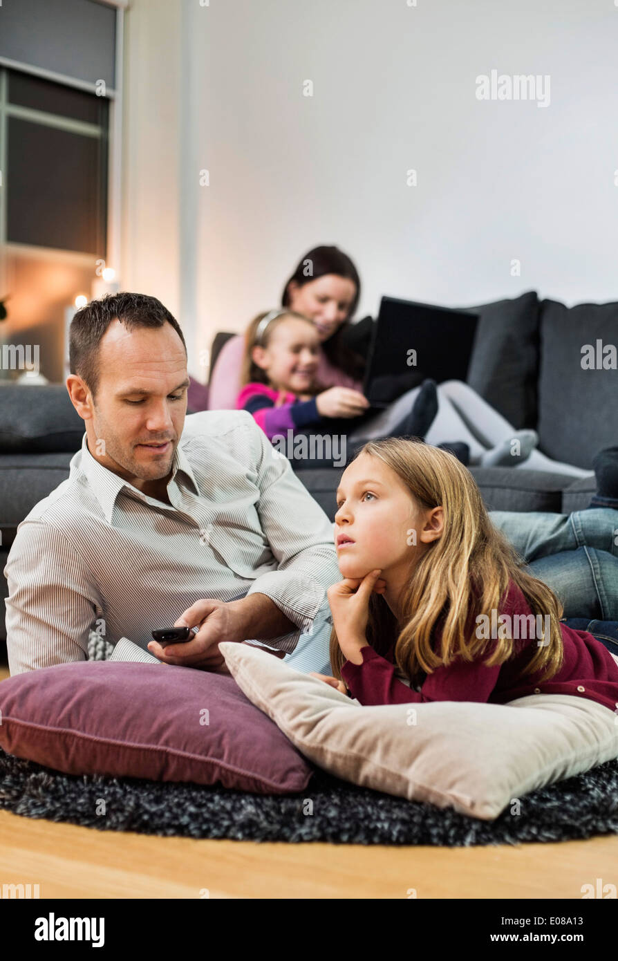 Father and daughter watching TV on floor with family in background ...