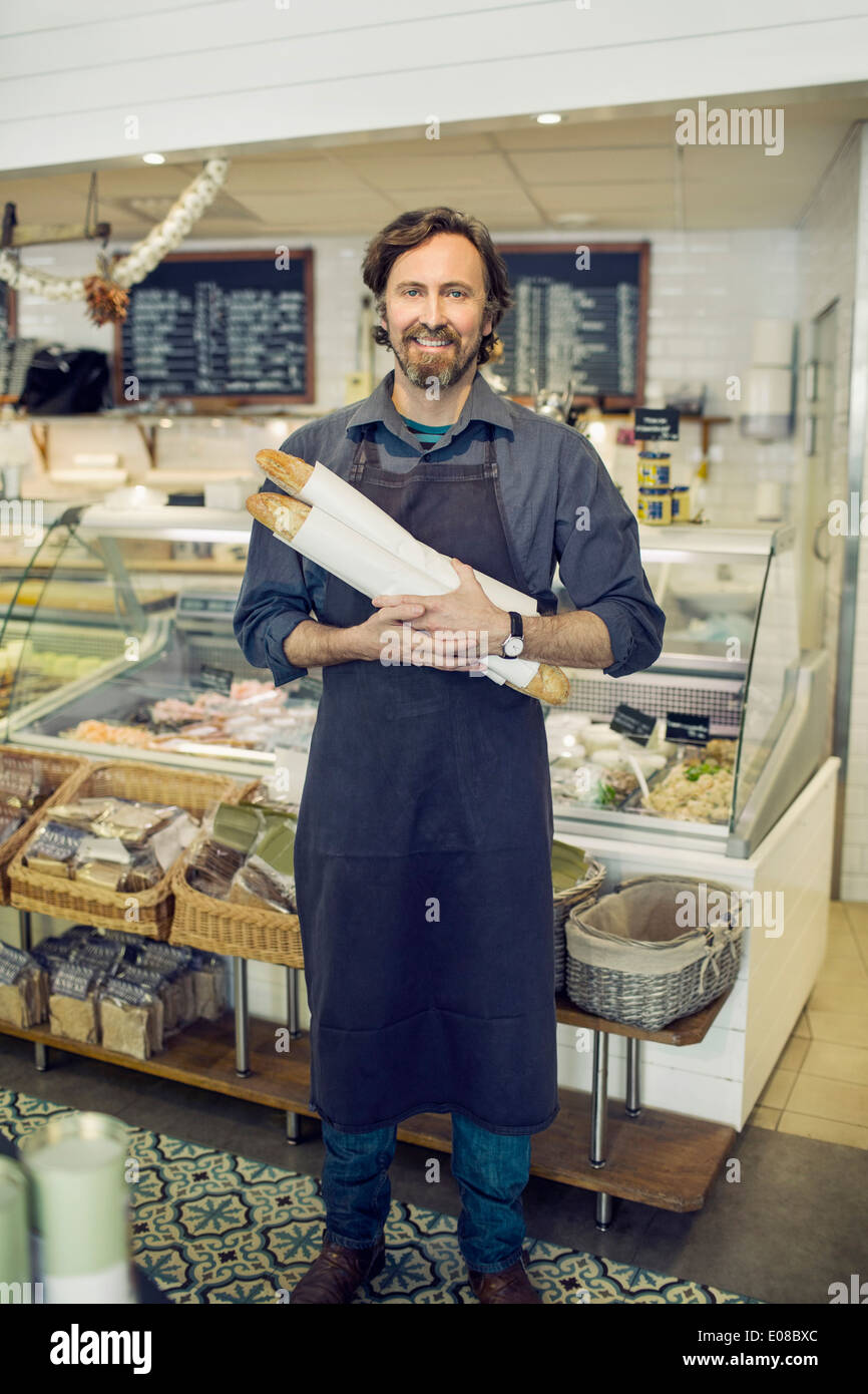 Portrait of mature male baker holding loaves of bread in supermarket ...