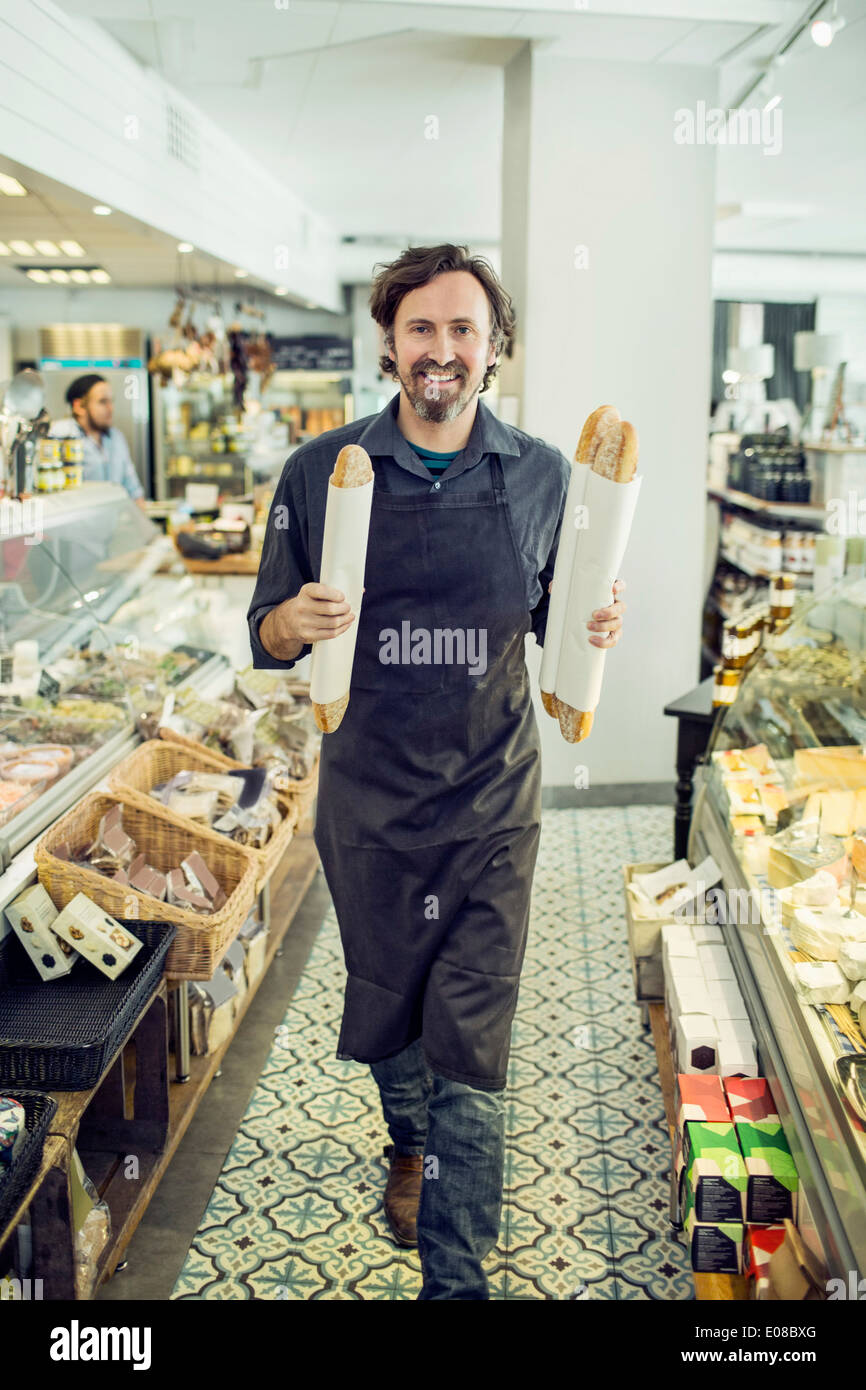 Portrait of mature male baker with loaves of bread walking in ...