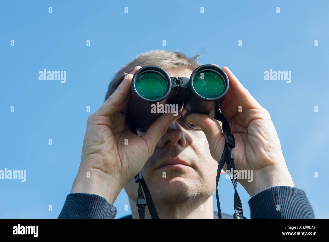 Male looking through binoculars with blue sky behind Stock Photo - Alamy