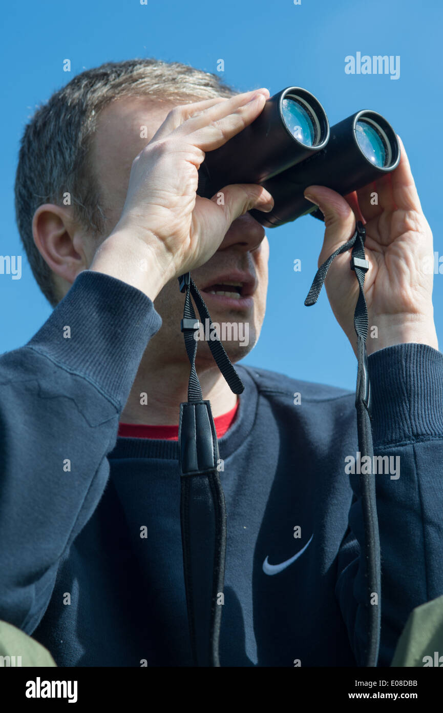 Male looking through binoculars with blue sky behind Stock Photo - Alamy