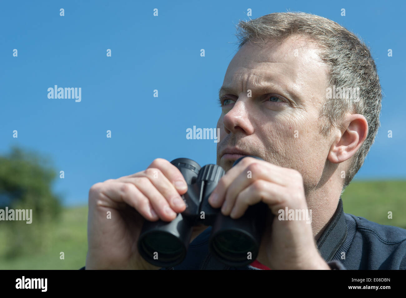Male using binoculars with blue sky behind Stock Photo - Alamy