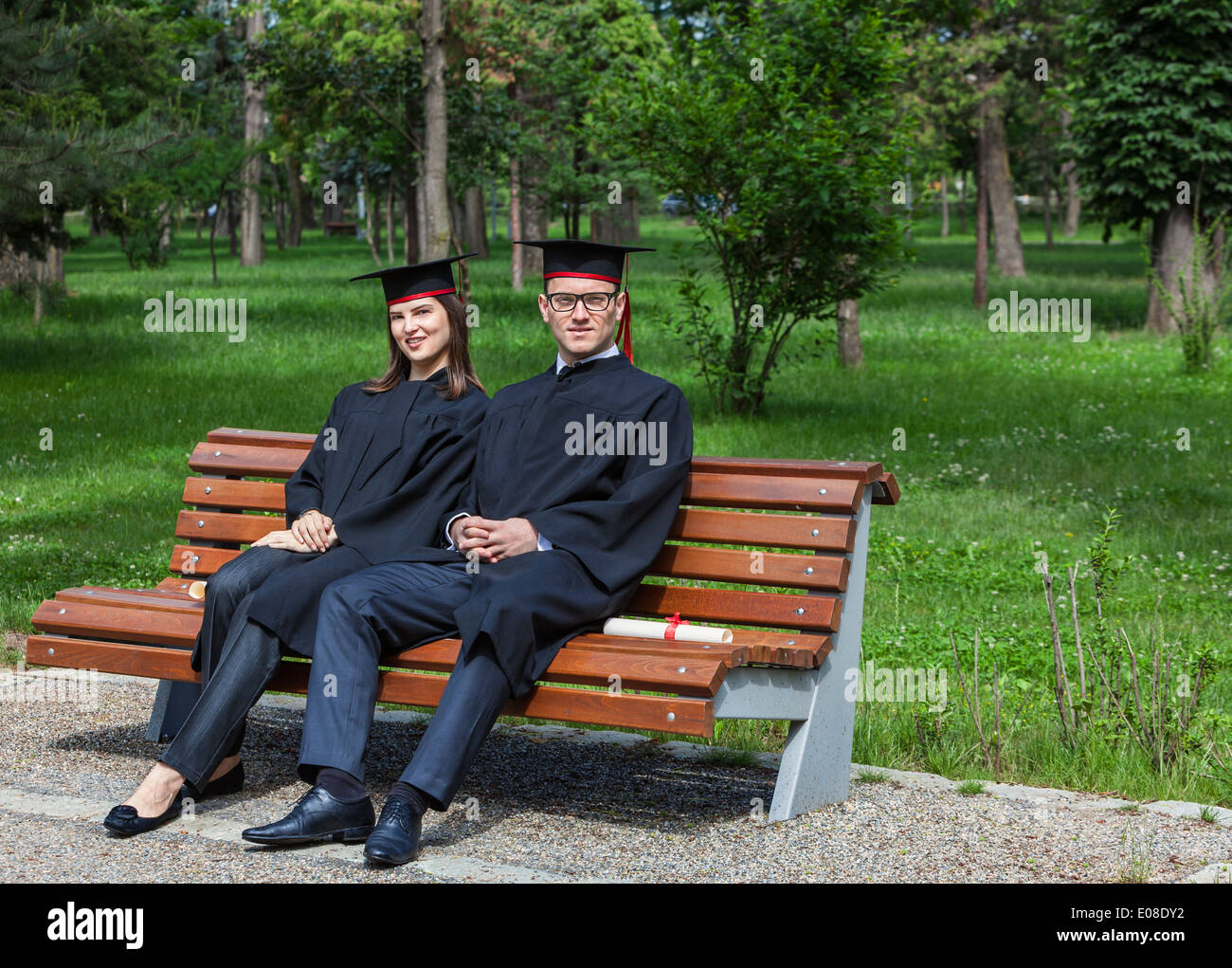 Portrait of a couple in the graduation day siting on a bench in a park ...