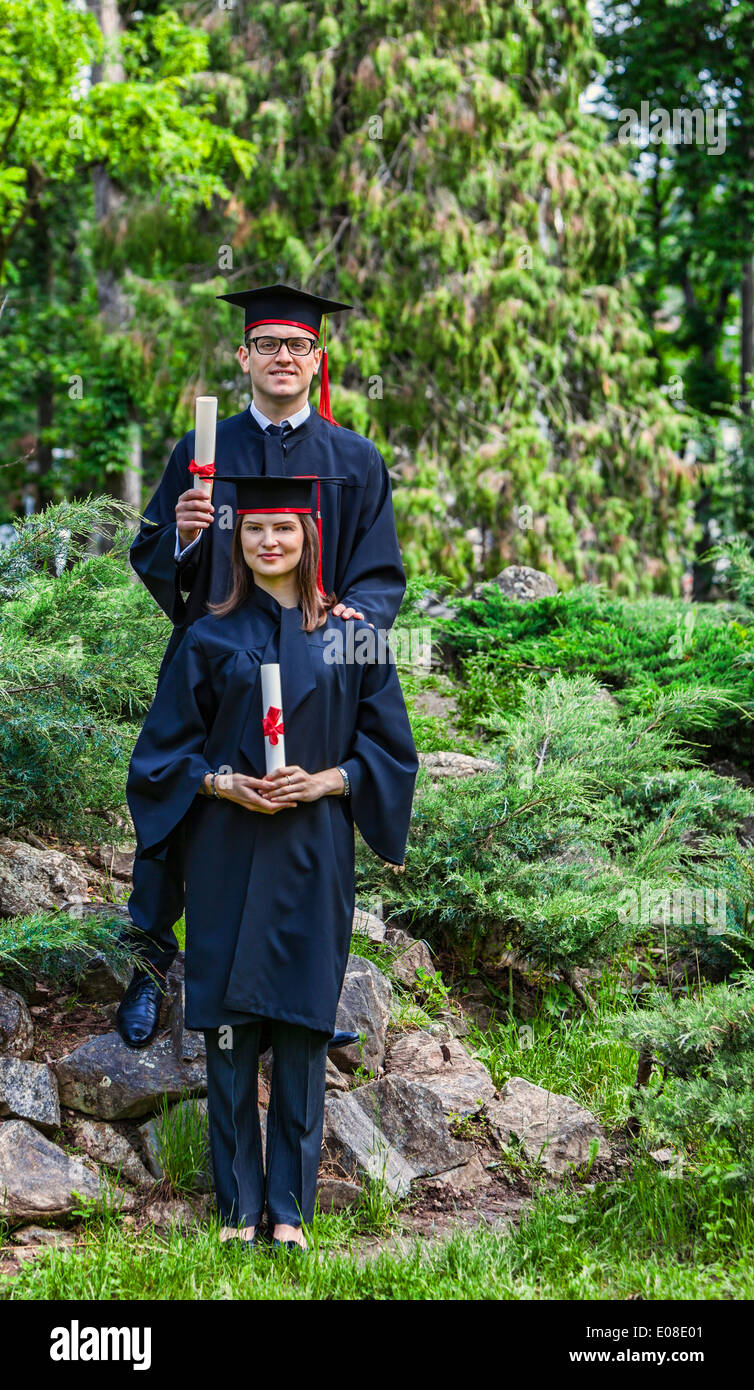 Young couple in the graduation day posing outdoor in a beautiful green ...