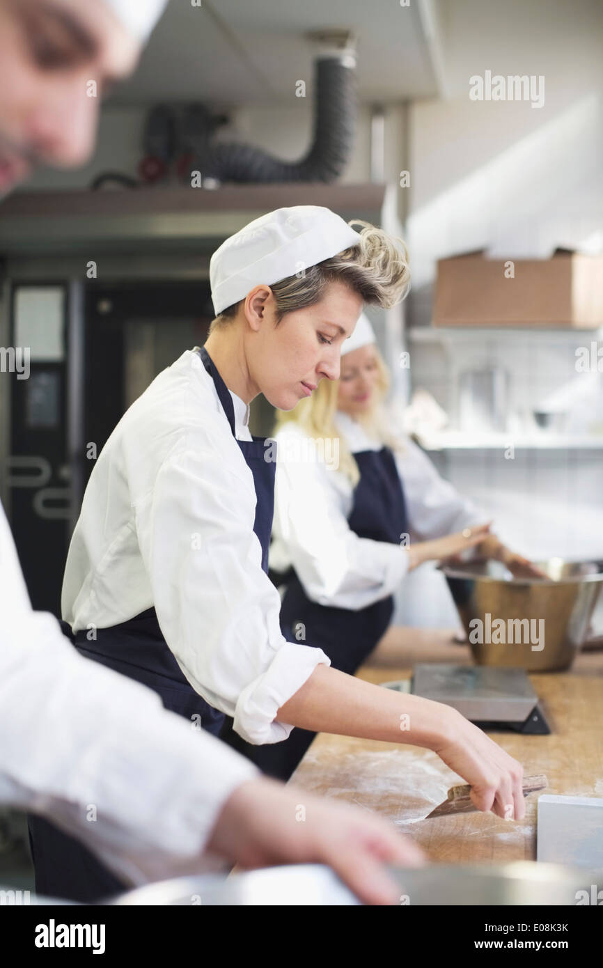 Side view of female baker baking with colleagues in commercial kitchen ...