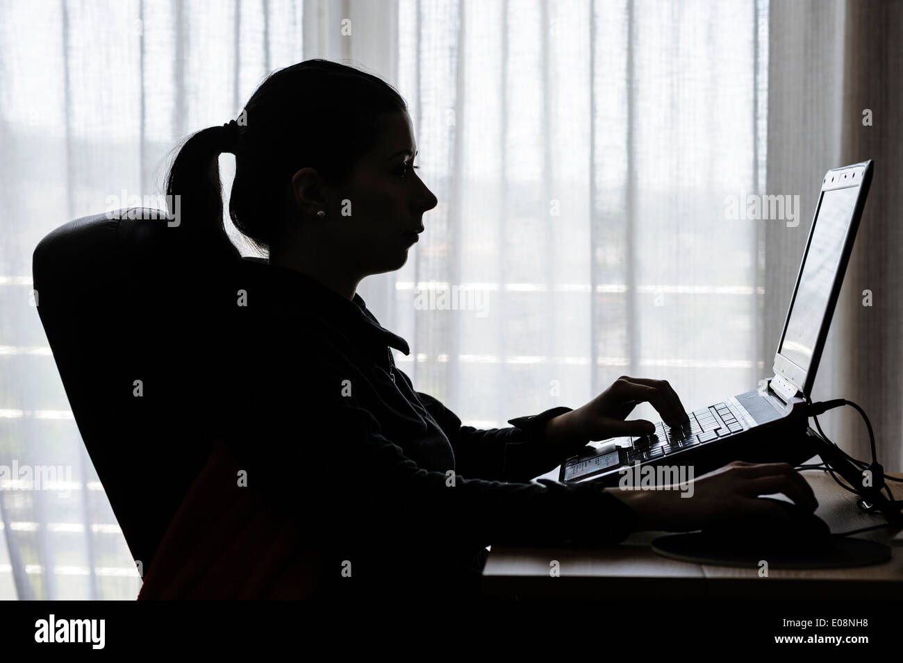 Silhouette of a young woman using a laptop computer at home Stock Photo ...