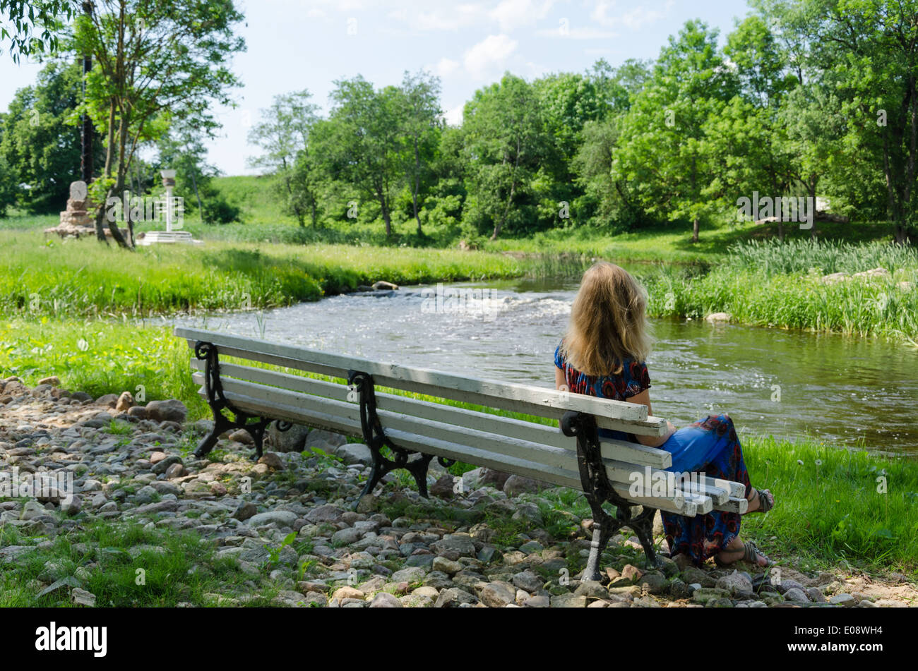 beautiful woman sitting on white bench beside a fast flowing stream ...