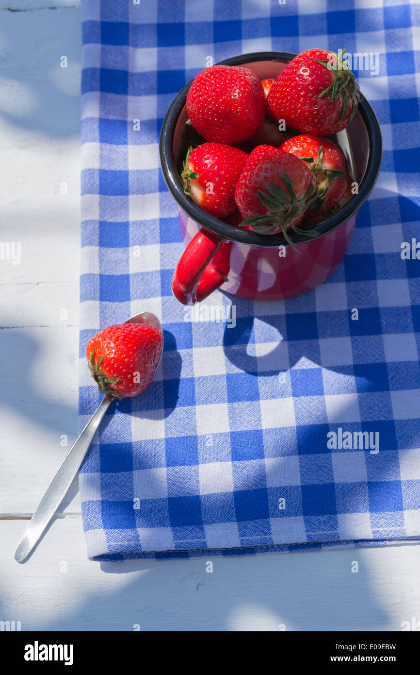 A small red pot filled with strawberries, one more strawberry and spoon ...