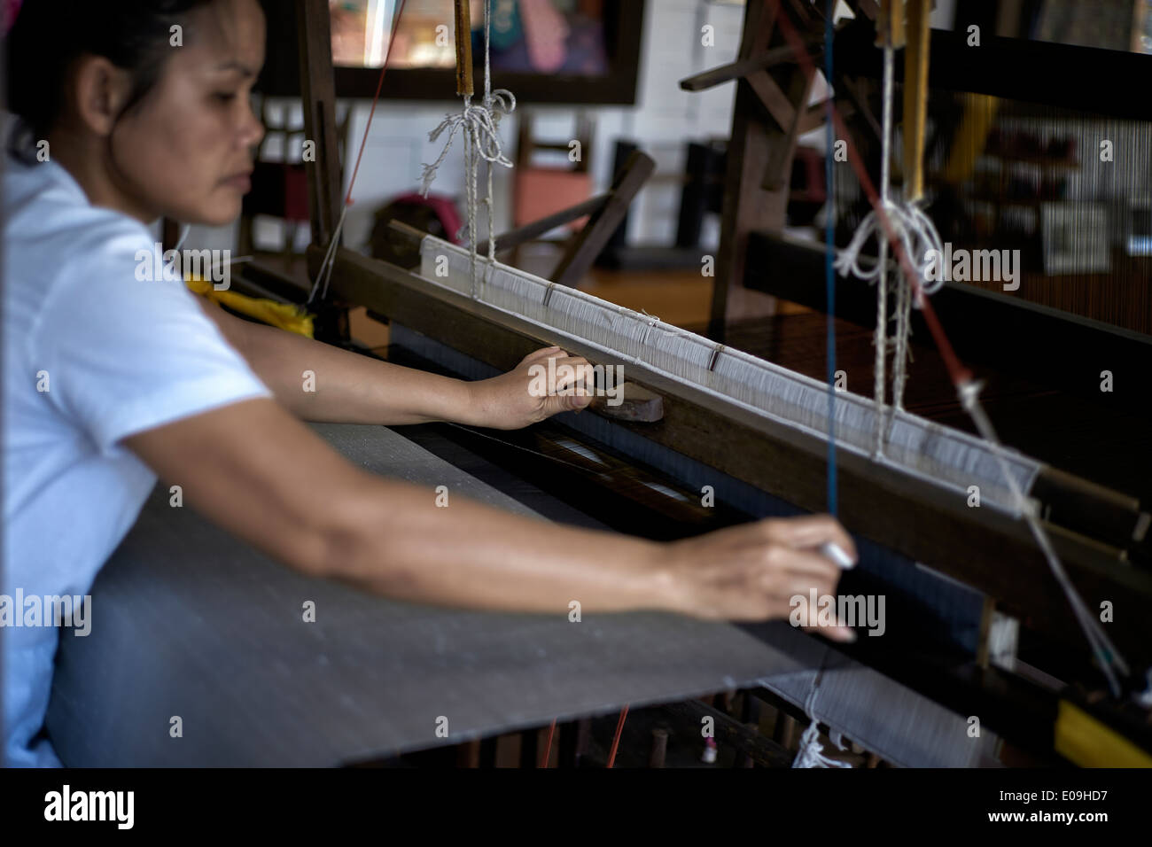 Thai woman working at a traditional wooden weaving loom producing woven ...