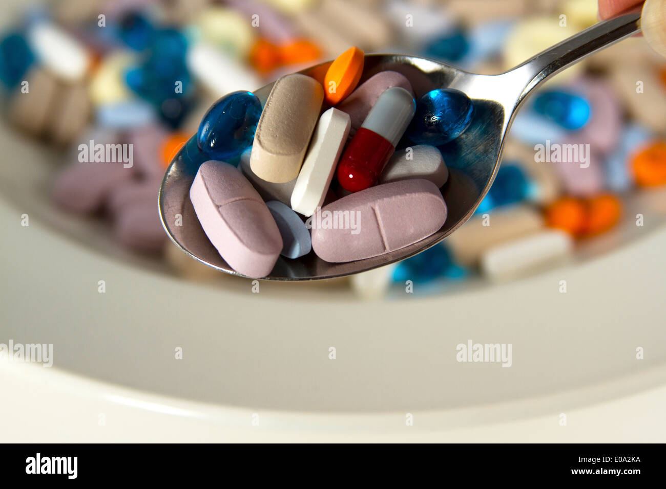 Spoon filled with pills and capsules with a background of a bowl full ...