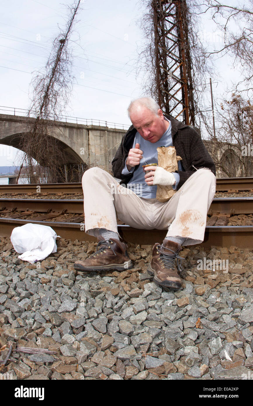 Homeless man sitting on edge of railroad tracks eating from a tin can ...