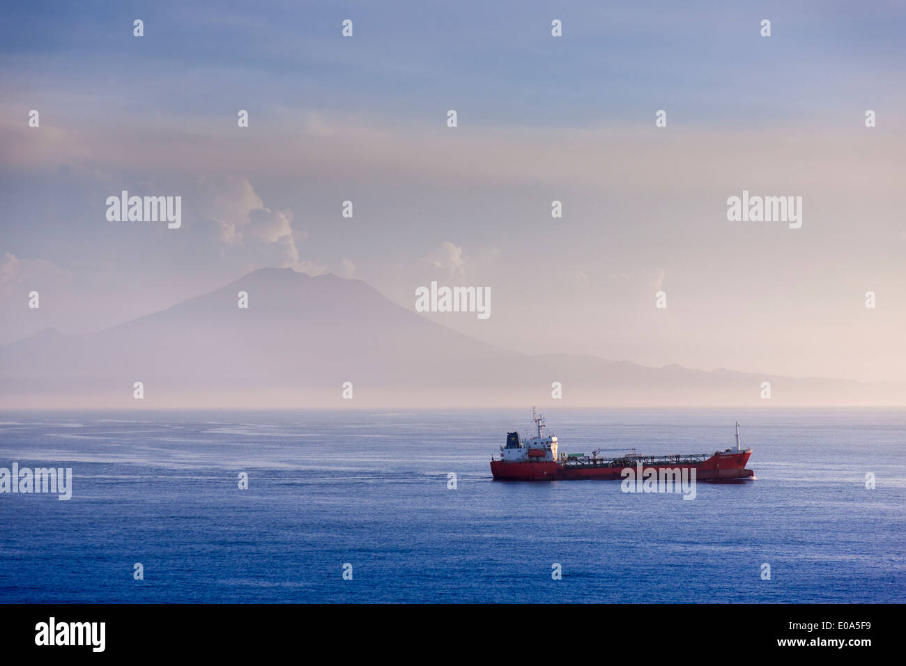Commercial ship with a smoking Volcano in the background, Indonesia ...