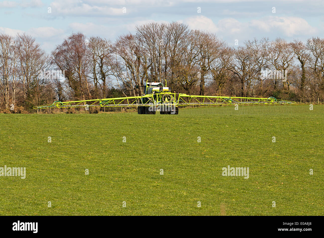 Farmer in tractor spraying fertilizer onto grass in field in spring ...