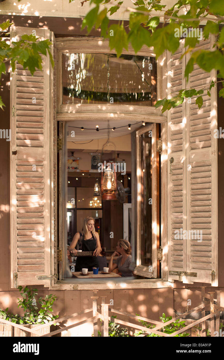Young woman serving coffee to customer, viewed through coffee shop ...