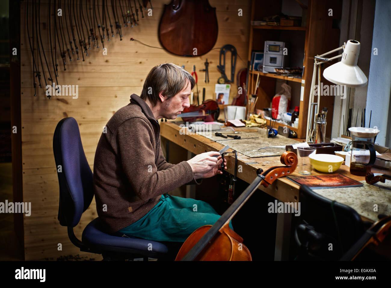 Violin maker in his workshop filing a cello mechanism Stock Photo - Alamy