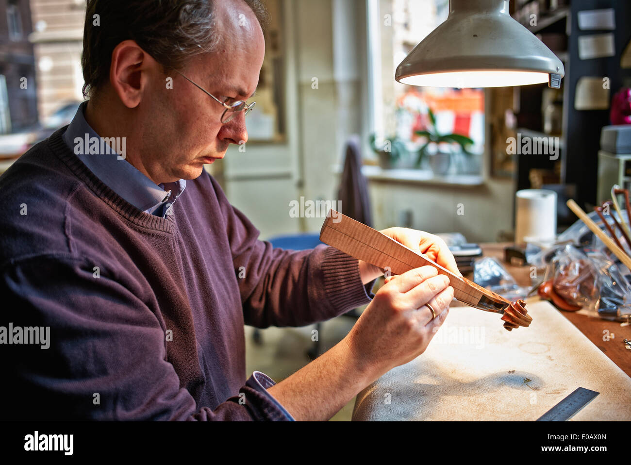 Violin maker in his workshop examining neck of an instrument Stock ...