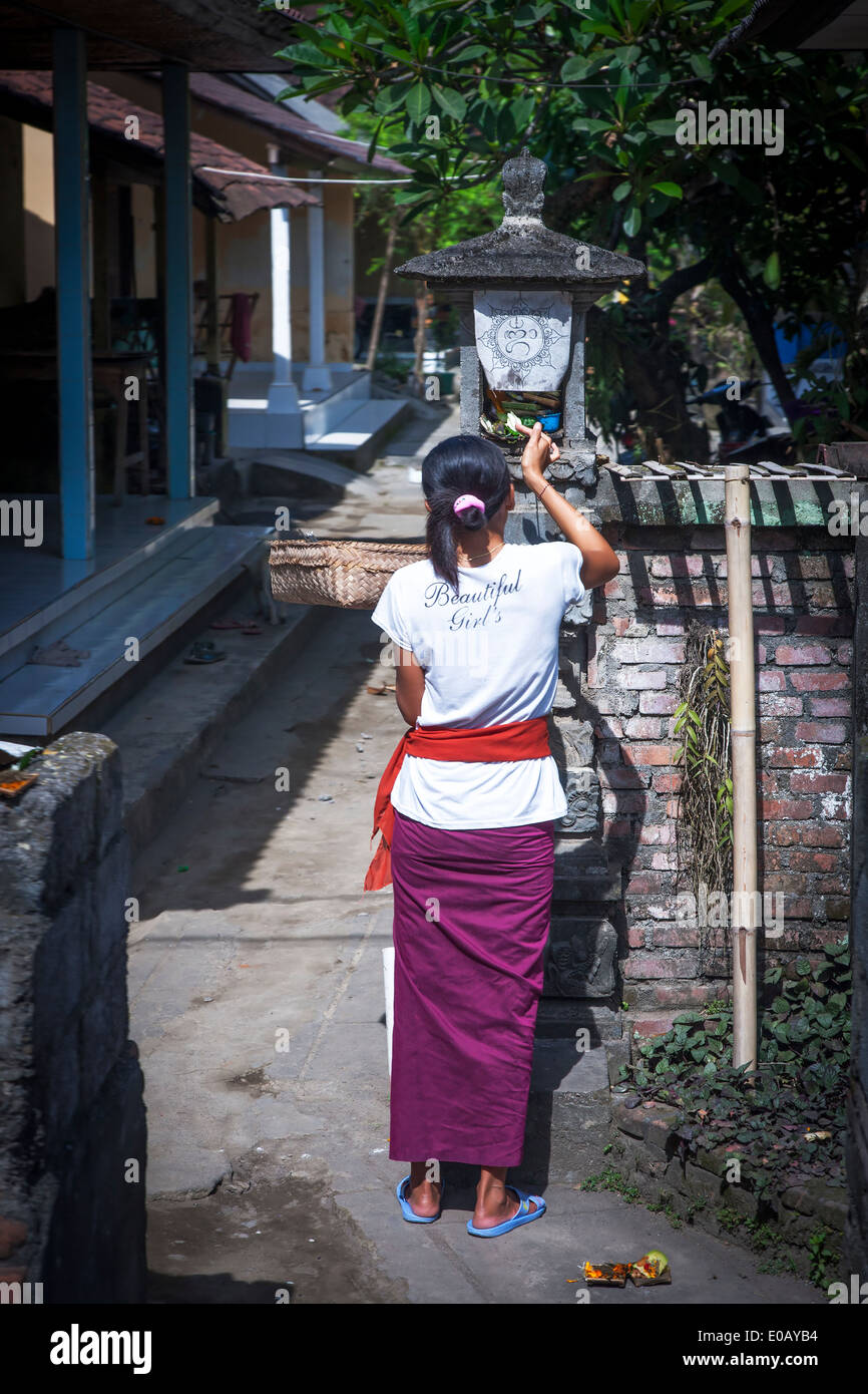 Young women putting a offering out at a small temple at the entrance to ...