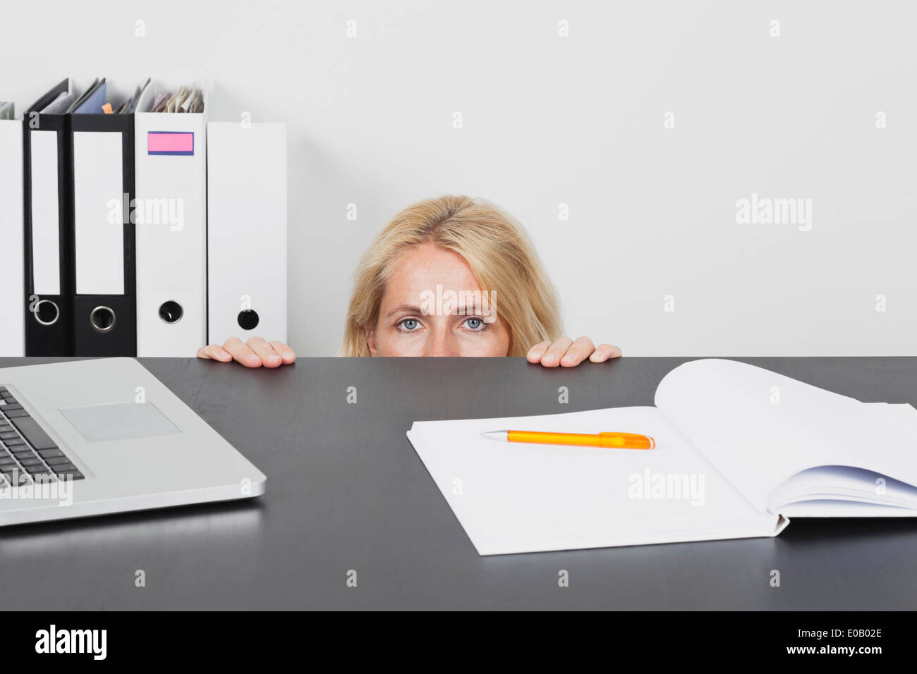 Businesswoman hiding behind desk Stock Photo - Alamy