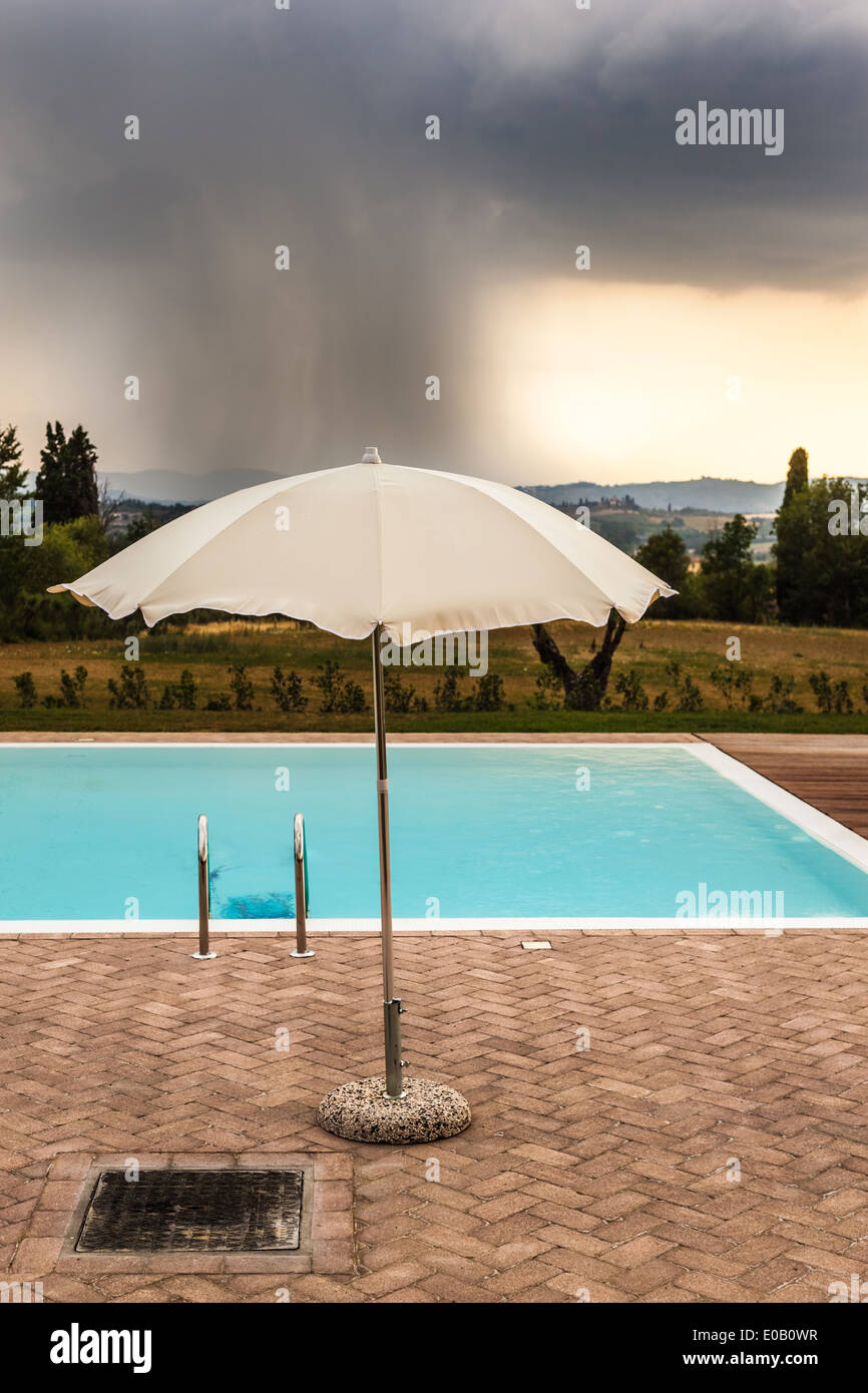 a parasol near the edge of a swimming pool and a storm in the ...