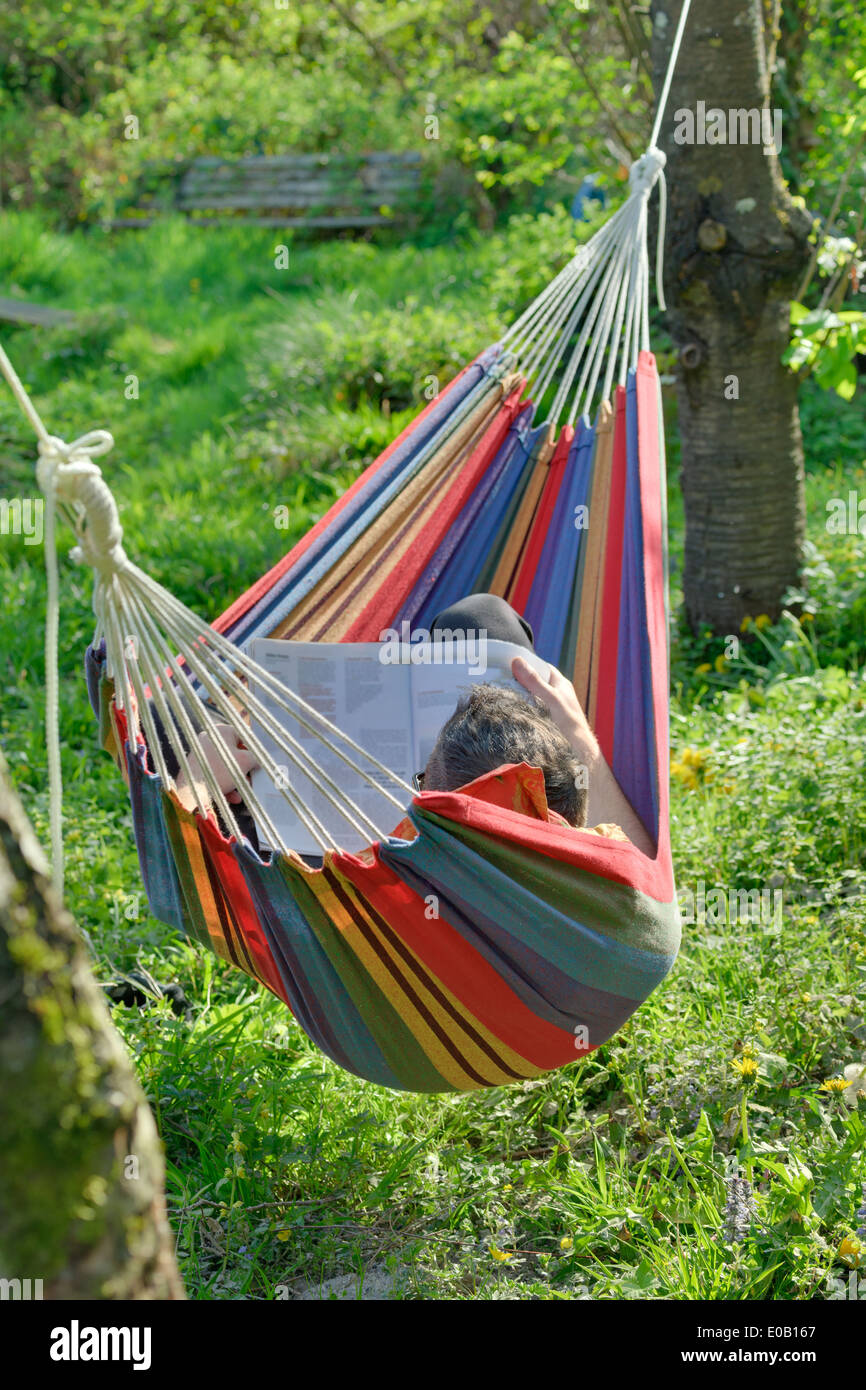 Germany, Young man lying in hammock and reading a magazine Stock Photo ...