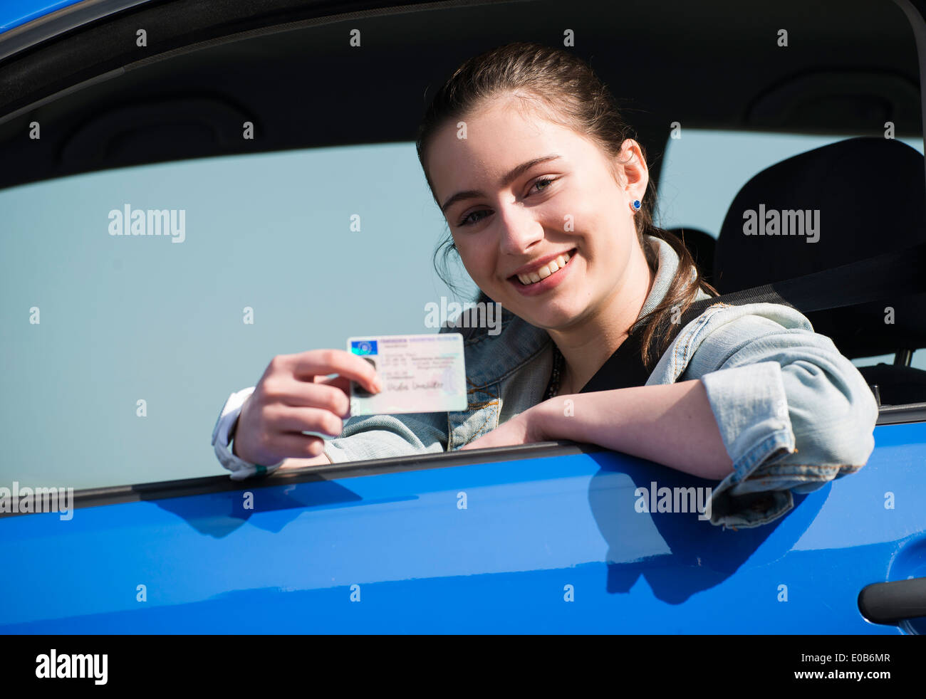 Smiling teenage girl sitting in car showing driving license, partial ...