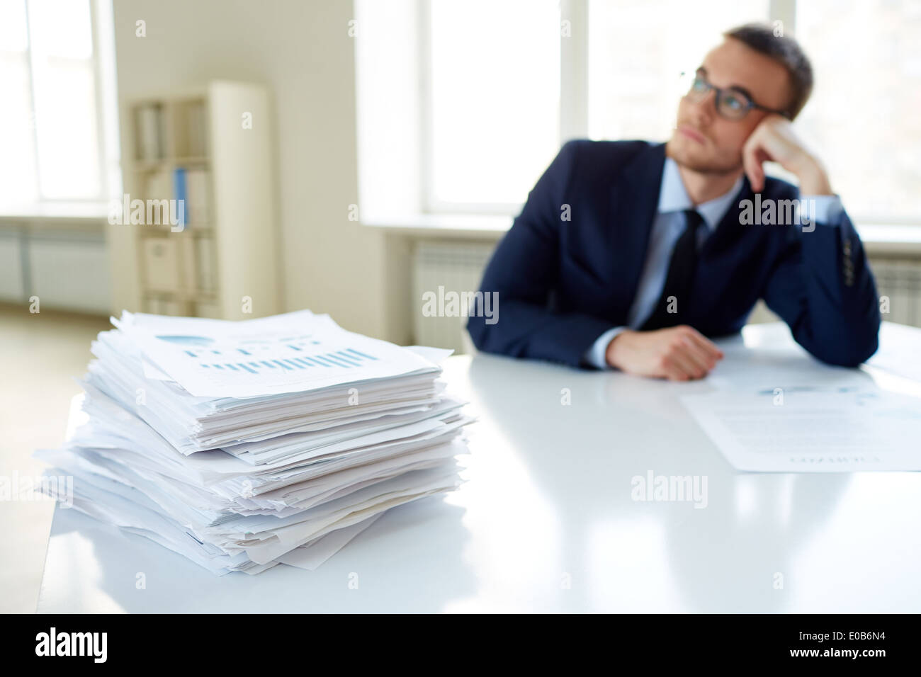 Stack of documents on the desk and pensive male employee working on ...
