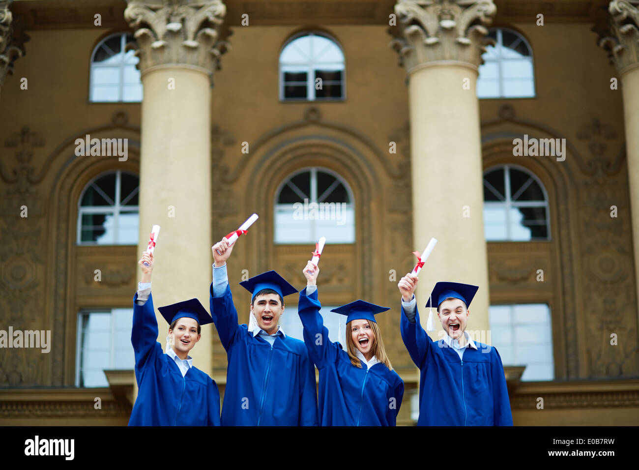 Group of smart students in graduation gowns showing their certificates ...
