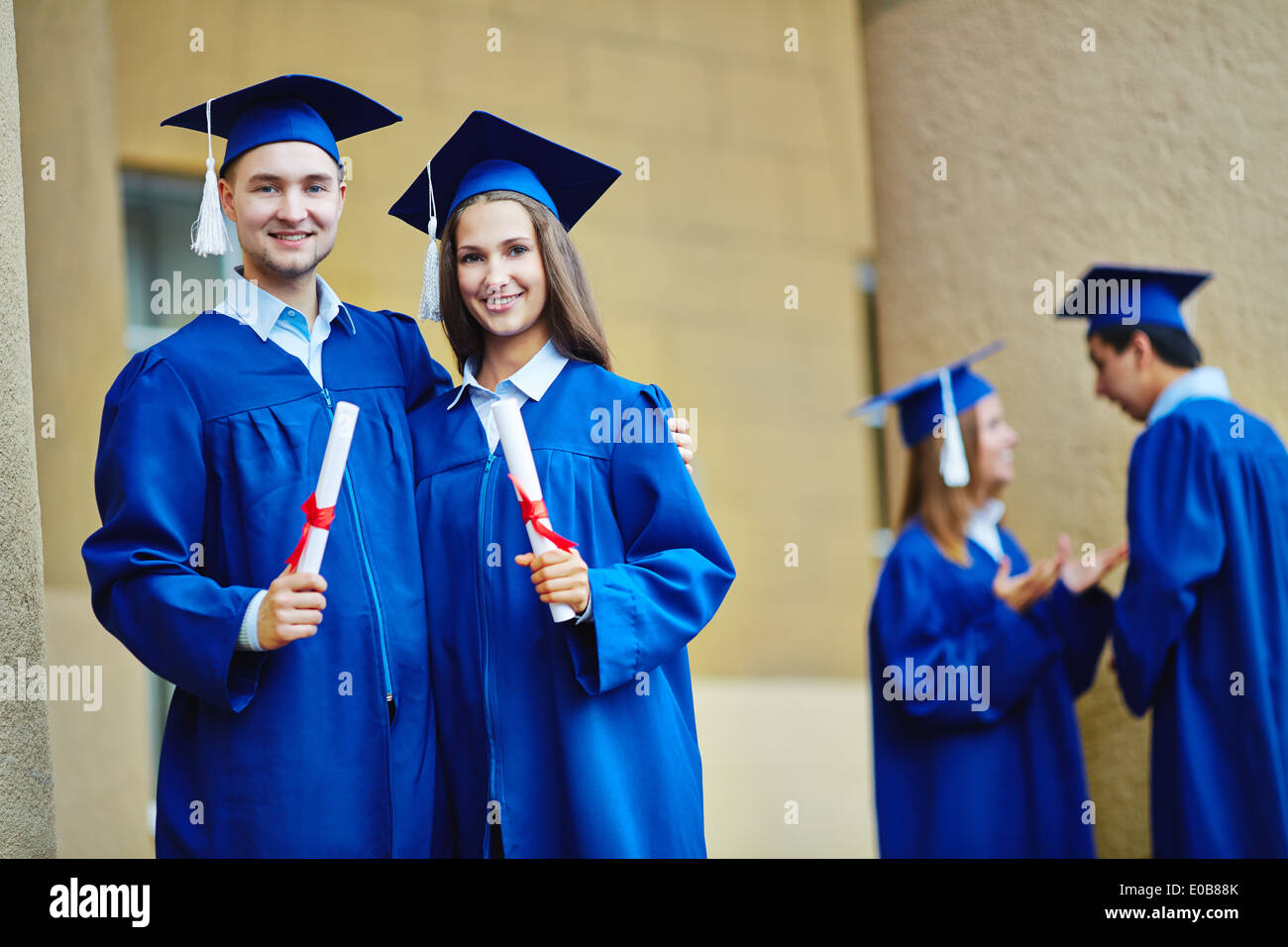 Two happy students in graduation gowns looking at camera with their ...