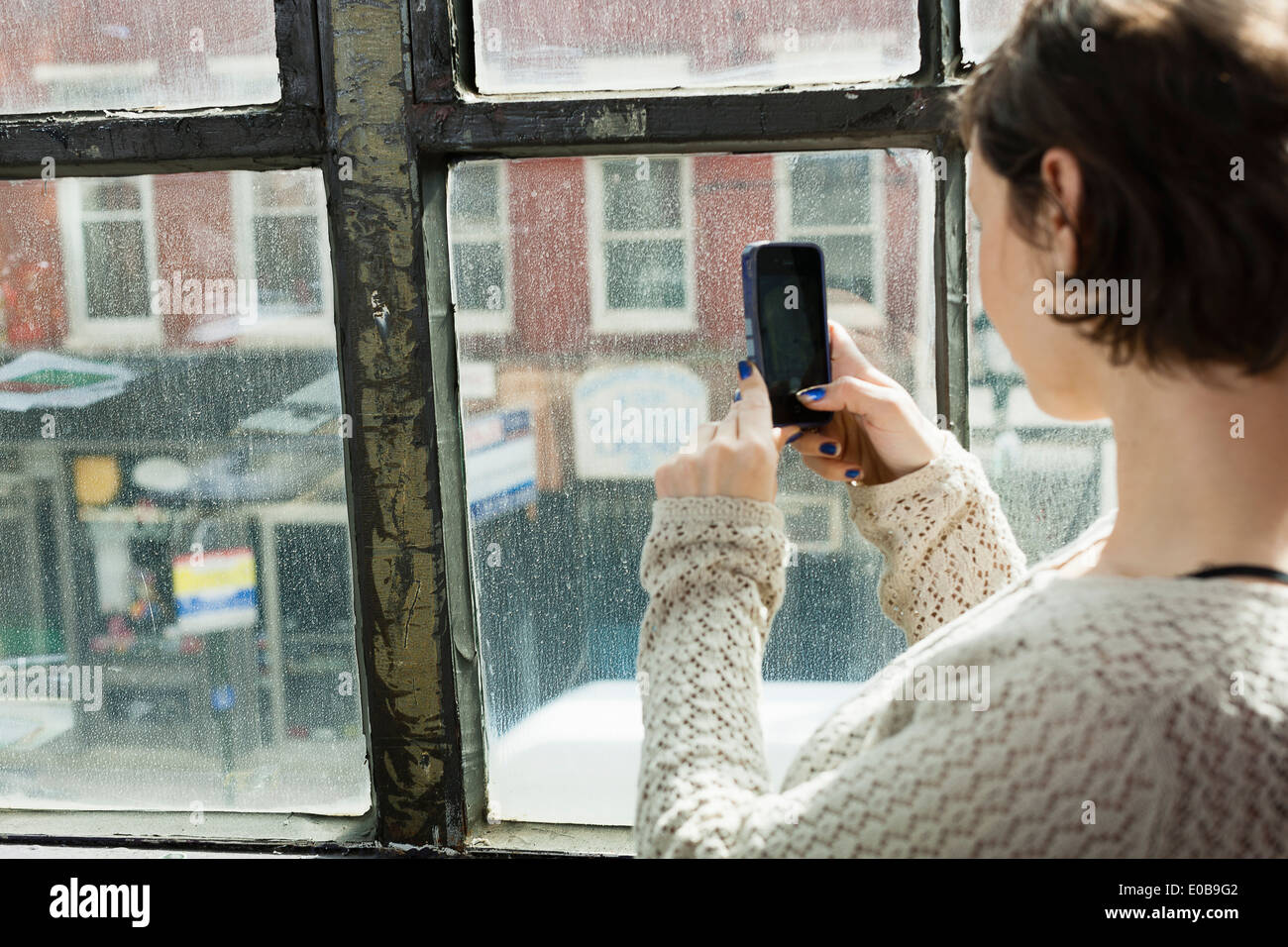 Young woman photographing street below from window Stock Photo - Alamy