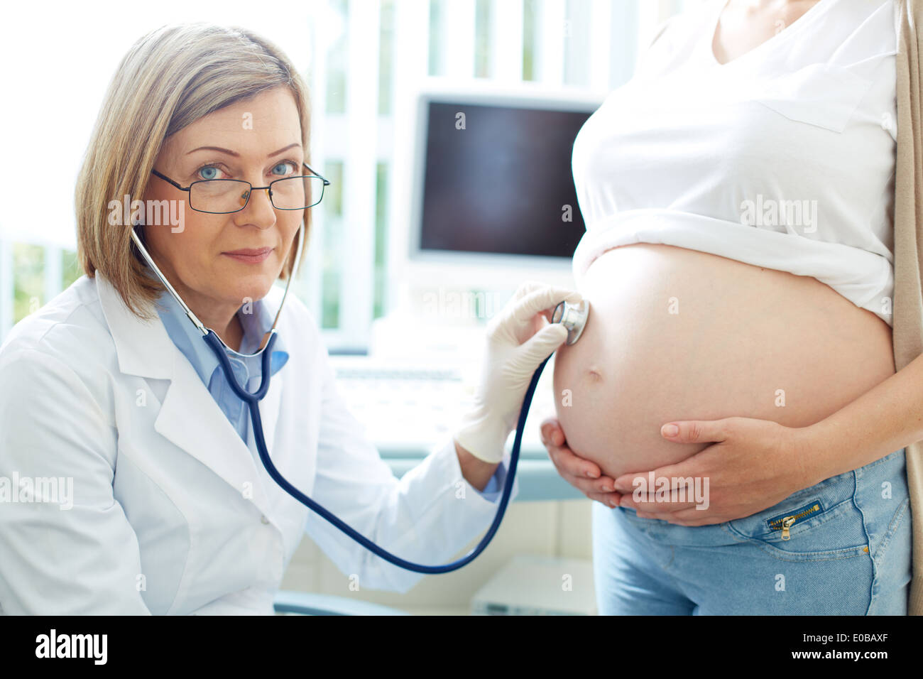 Mature gynecologist looking at camera while examining the belly of a ...