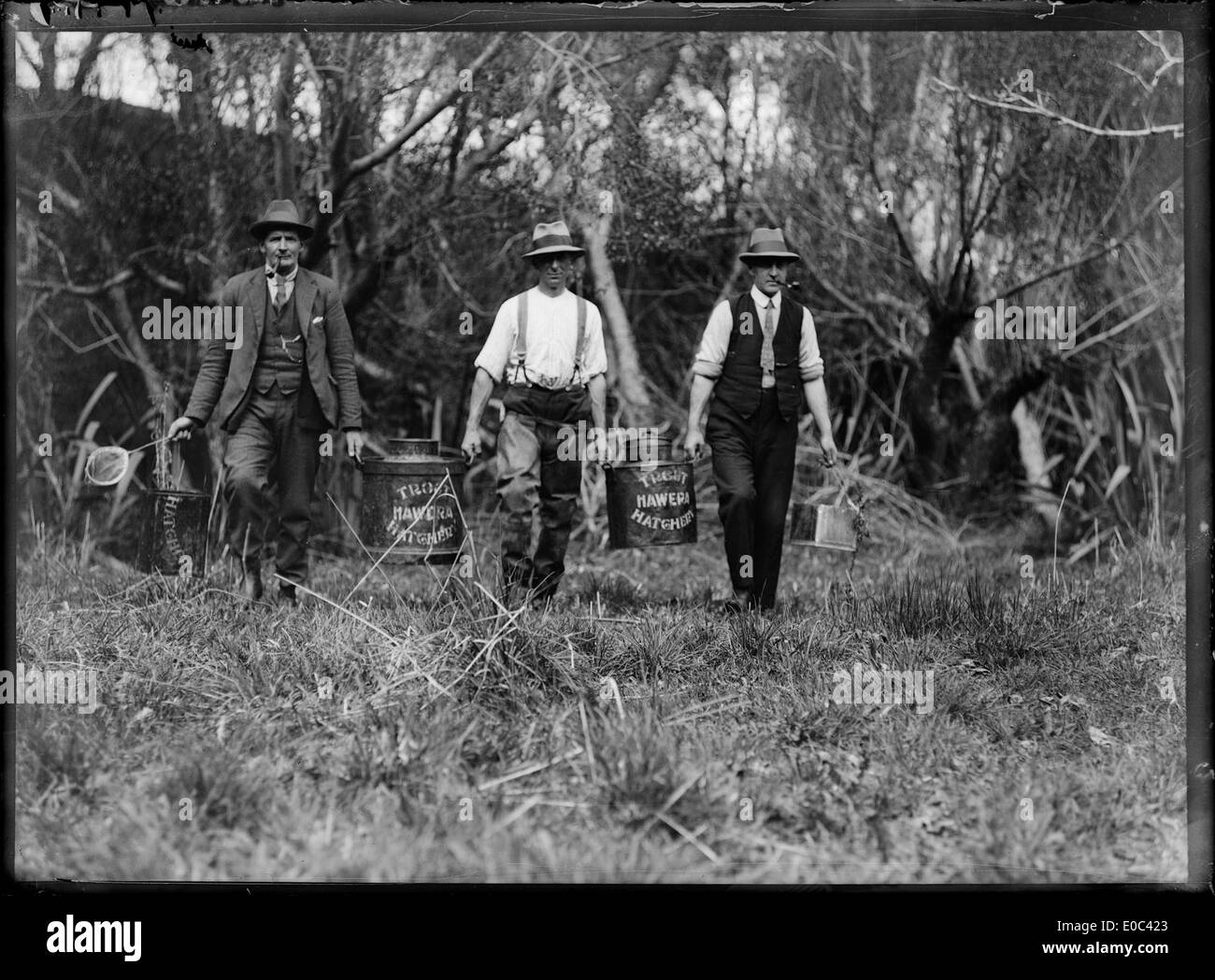 This historical photograph shows men carrying cans labeled with 'Hawera ...