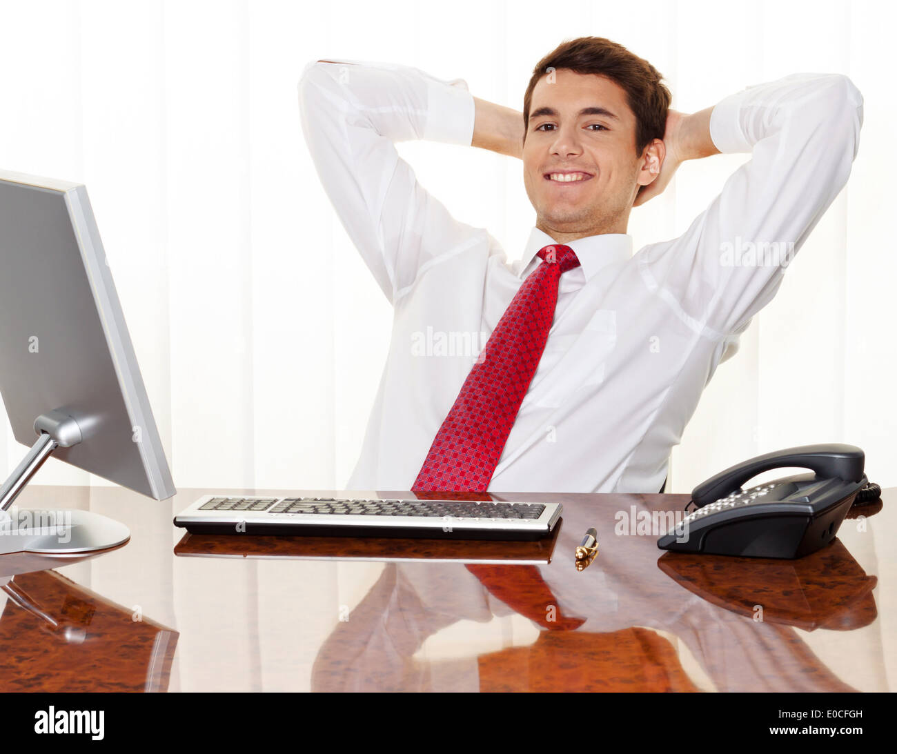 A successful young manager sits with desk and smiles., Ein ...