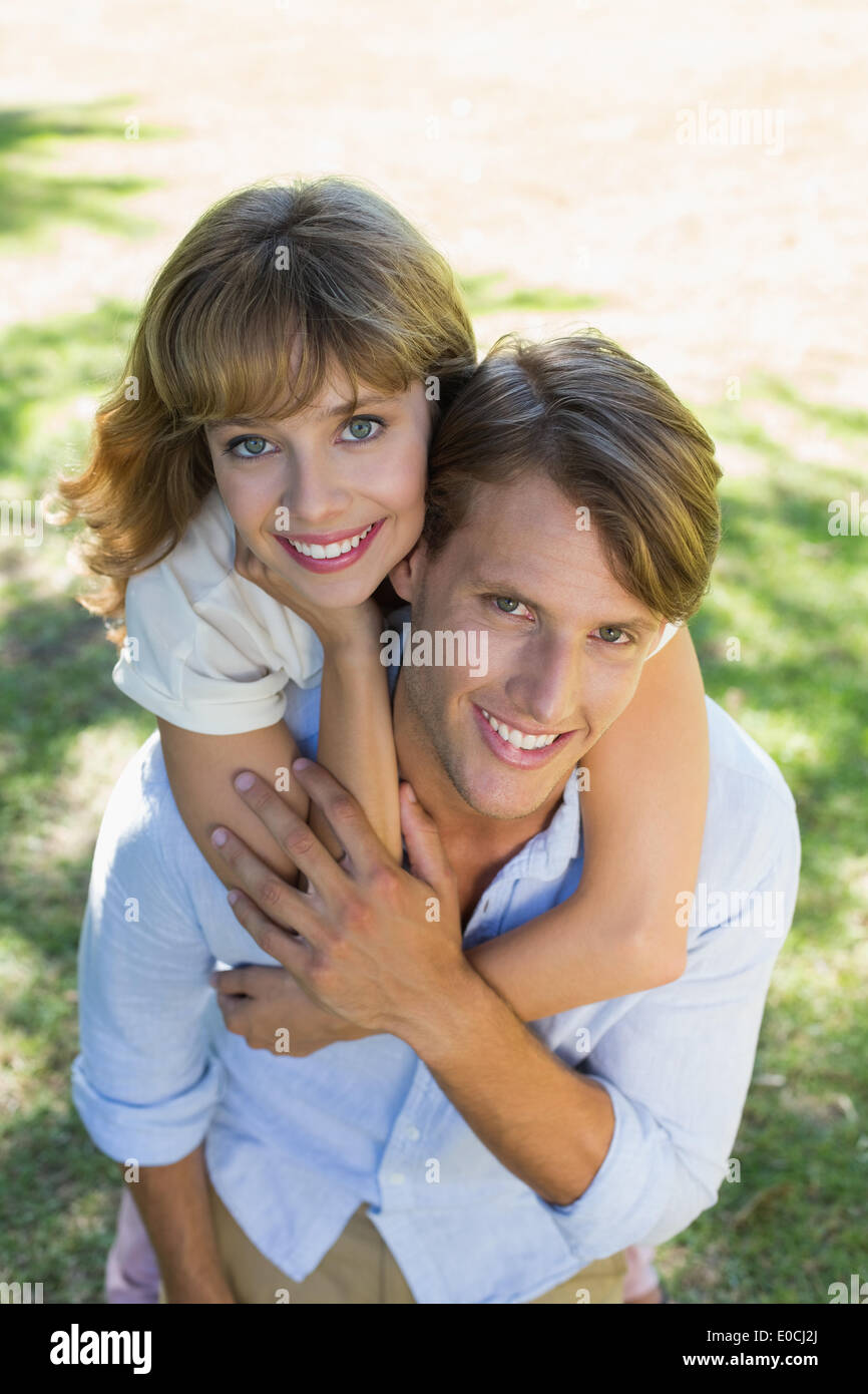 Man giving his pretty girlfriend a piggy back in the park smiling at ...