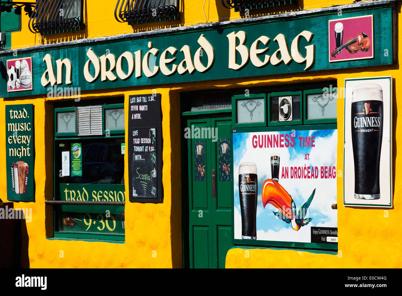 A bar with green and yellow facade and signs advertising beer; Dingle ...