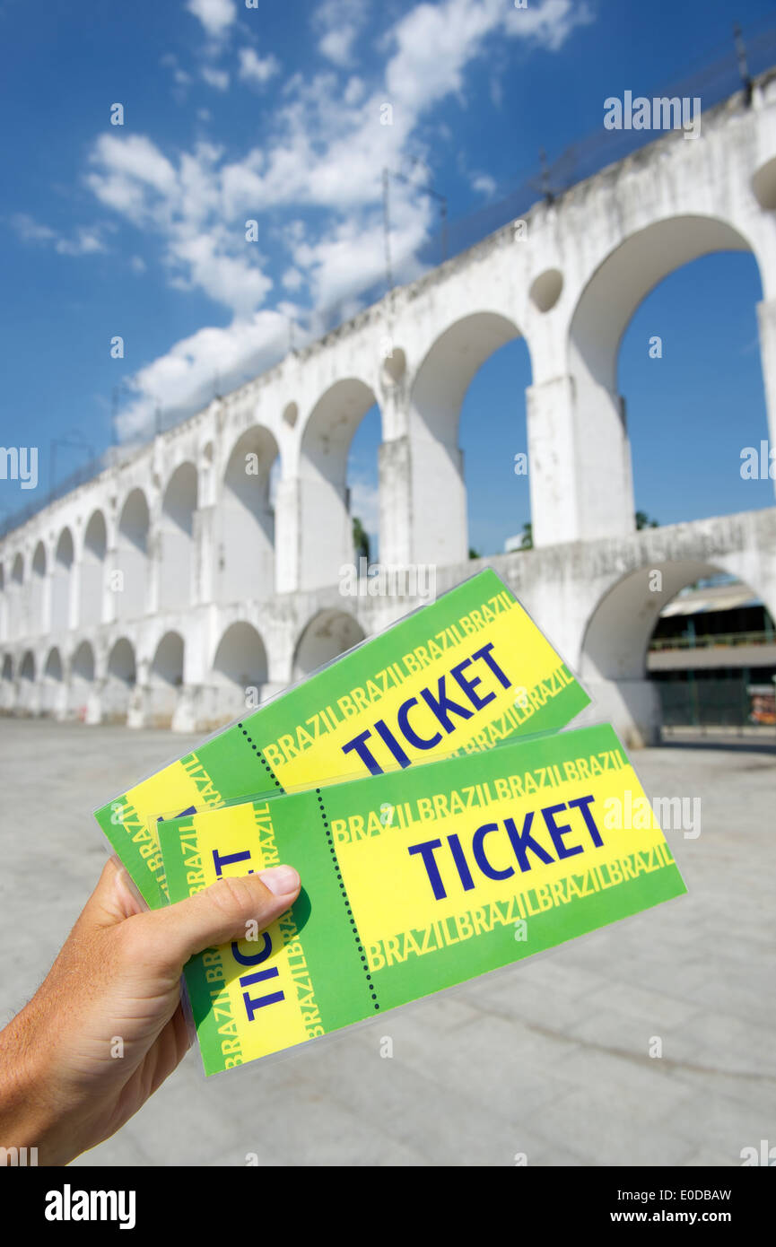 Hand holding two Brazil tickets in front of Arcos da Lapa Arches in ...