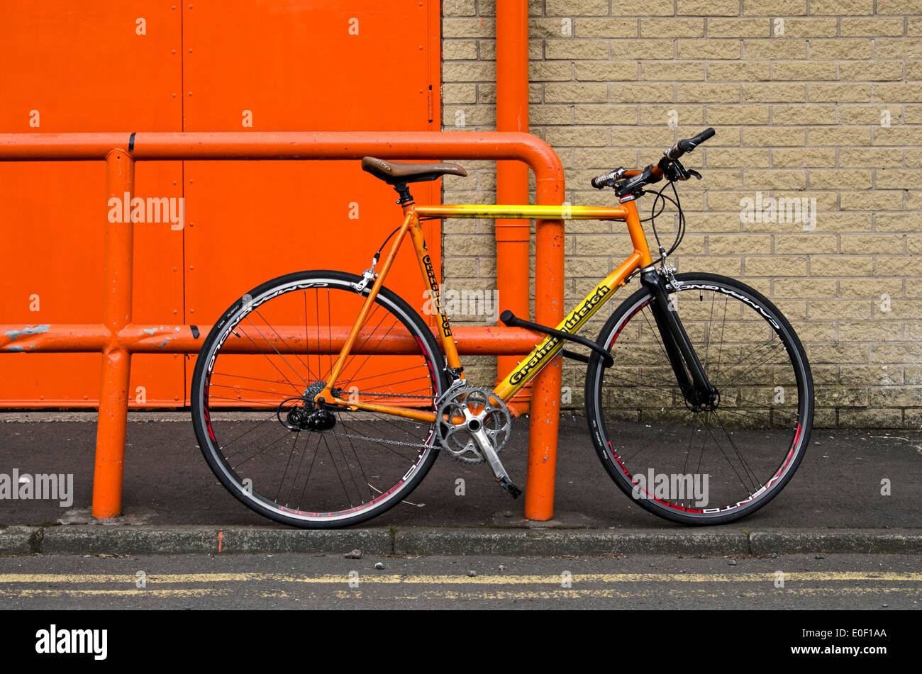 An orange and yellow coloured bicycle secured to an orange rail with an ...