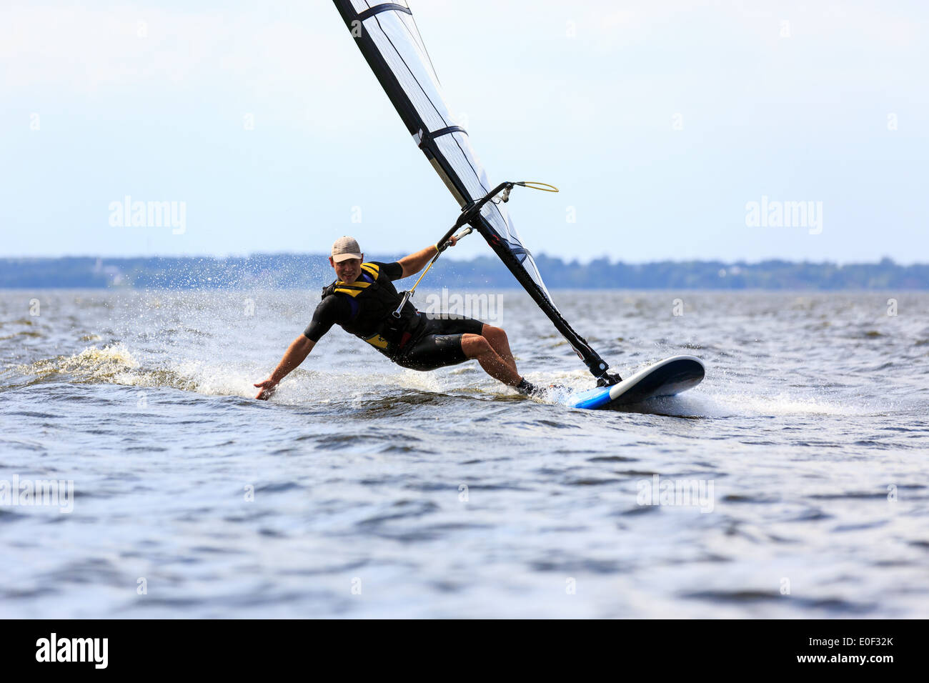 Young man surfing the wind and touching water surface with splashes ...