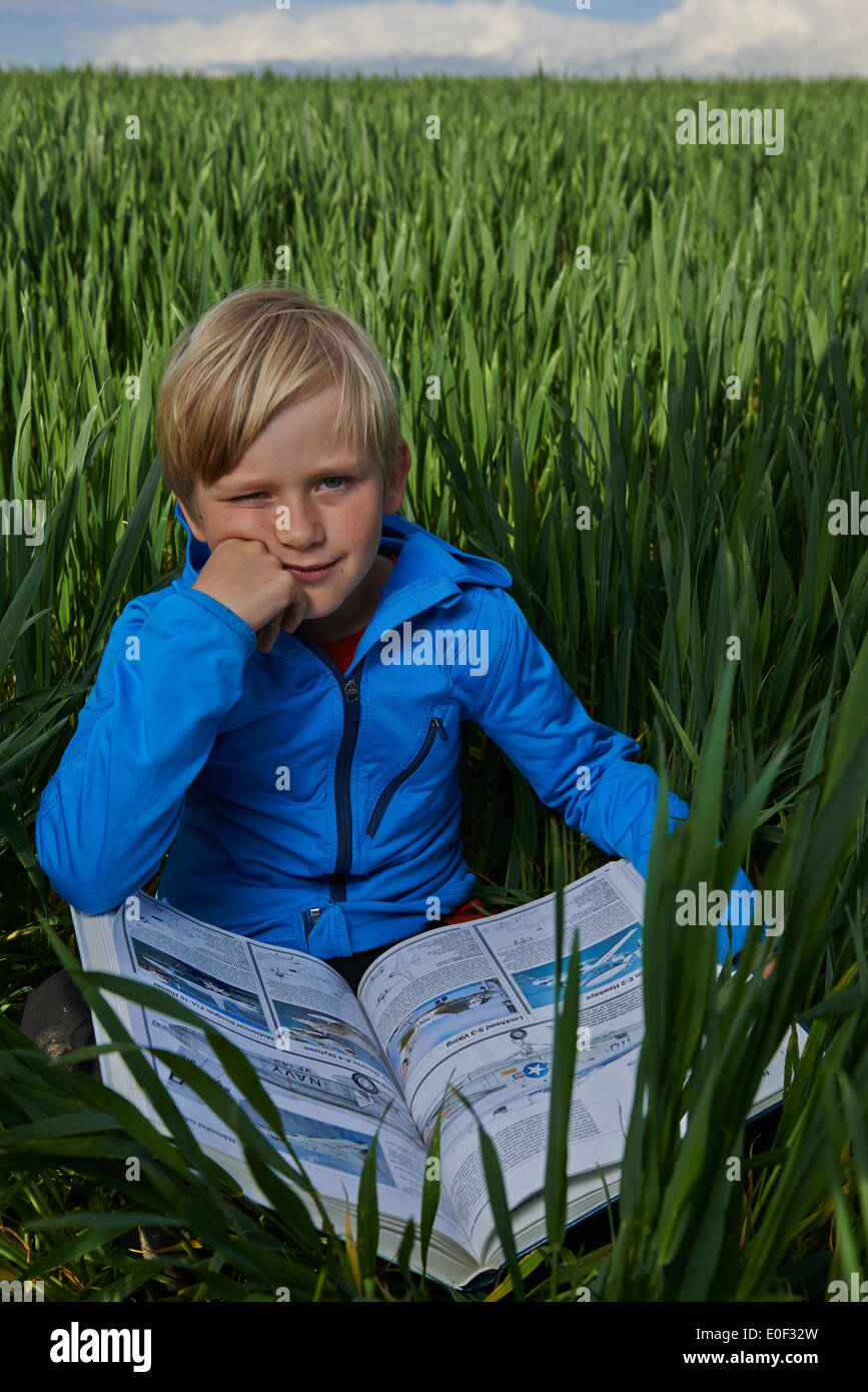 Closeup of a child blond boy reading a book outside in high green grass ...