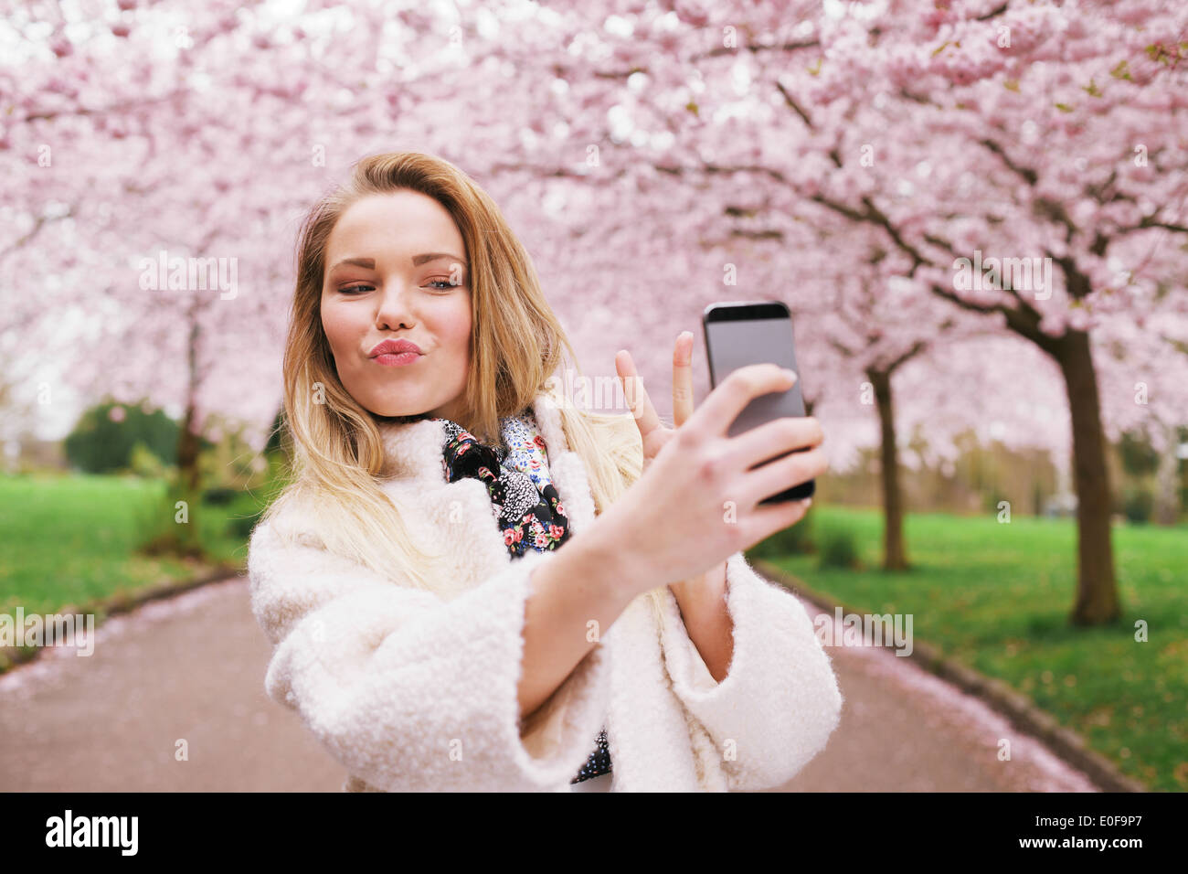 Cute young woman gesturing peace sign while taking her picture with ...