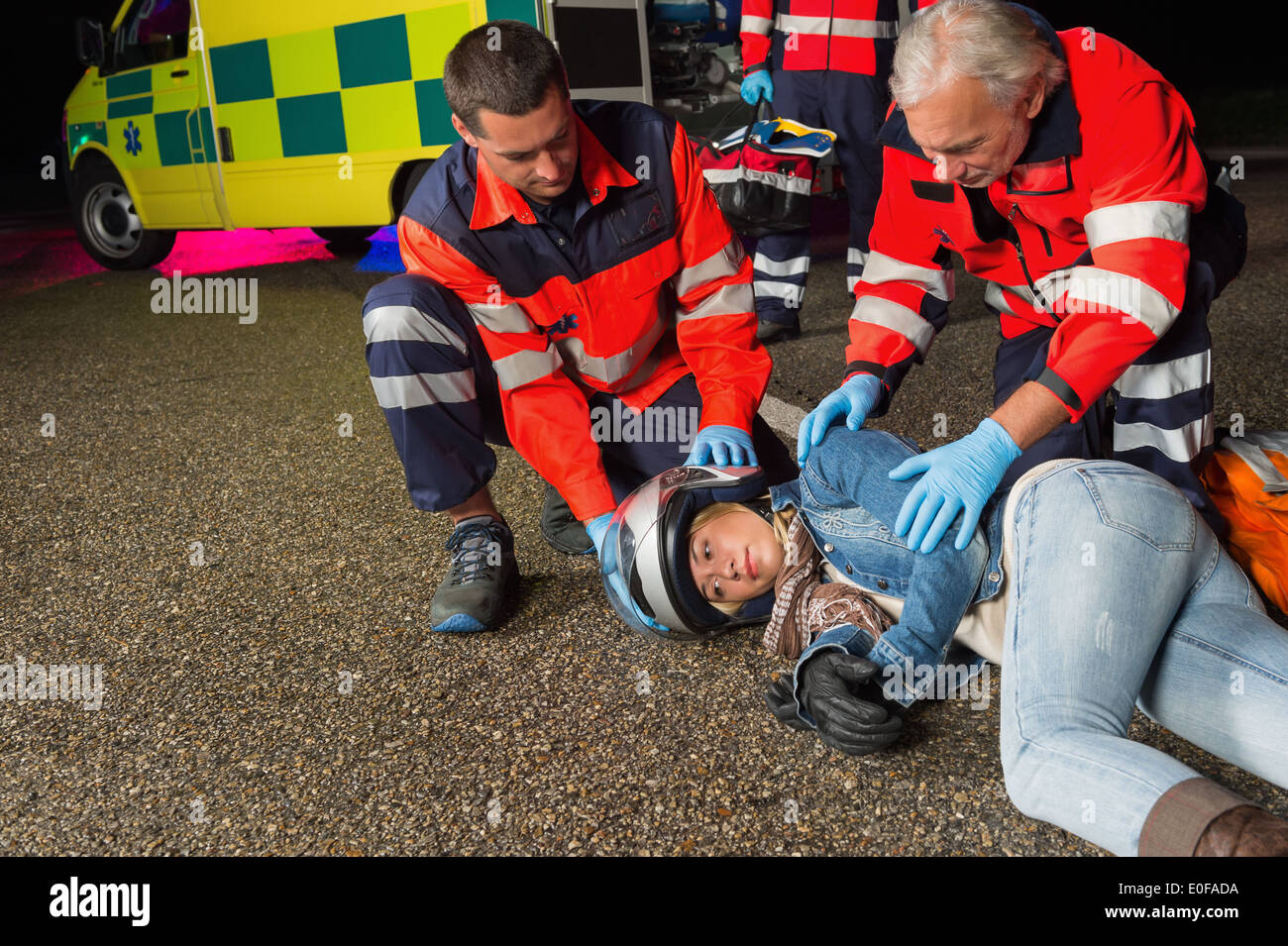 Paramedics helping injured motorbike woman driver lying on road night ...
