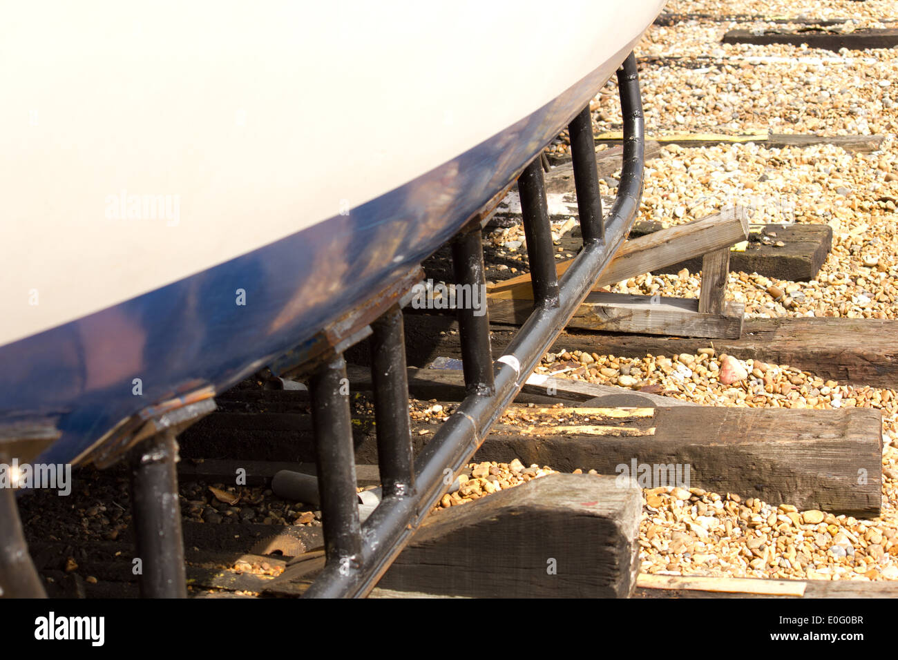 supported blue and white boat hull with wooden wedges on a shingled ...