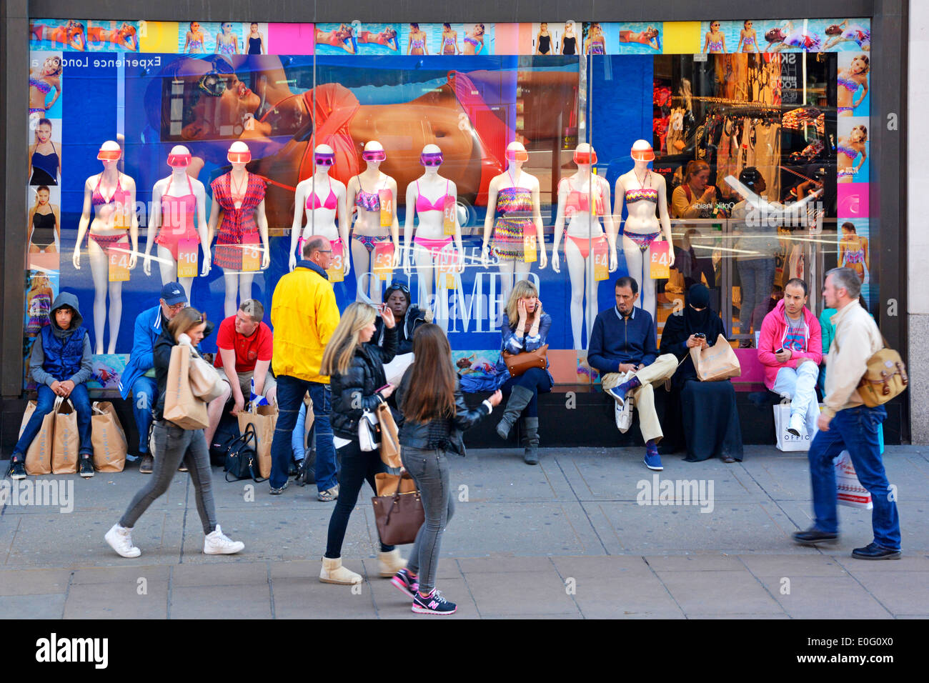 Shoppers outside Primark sitting on window sill with display of womans ...