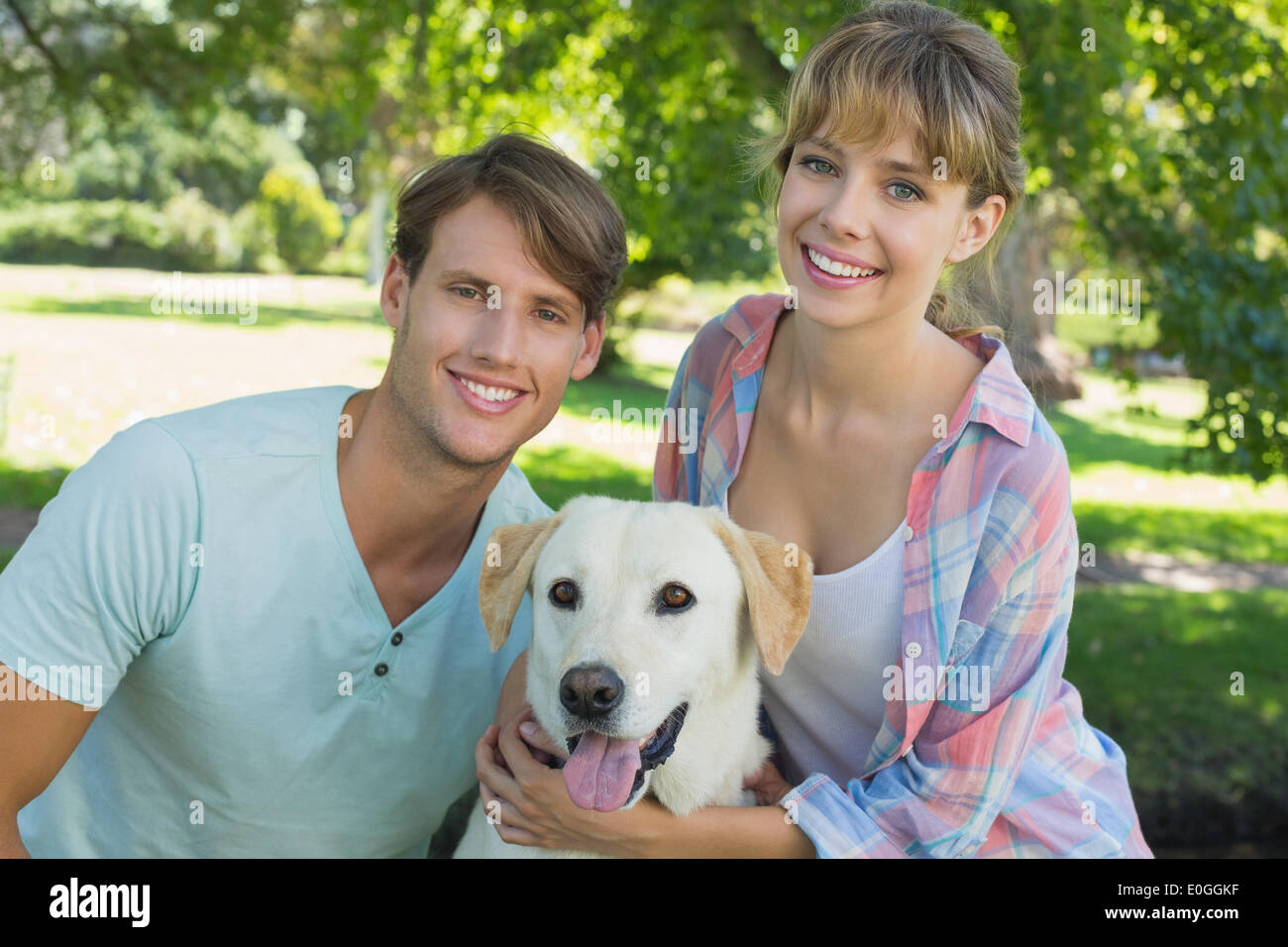 Happy couple sitting with their labrador in the park smiling at camera ...