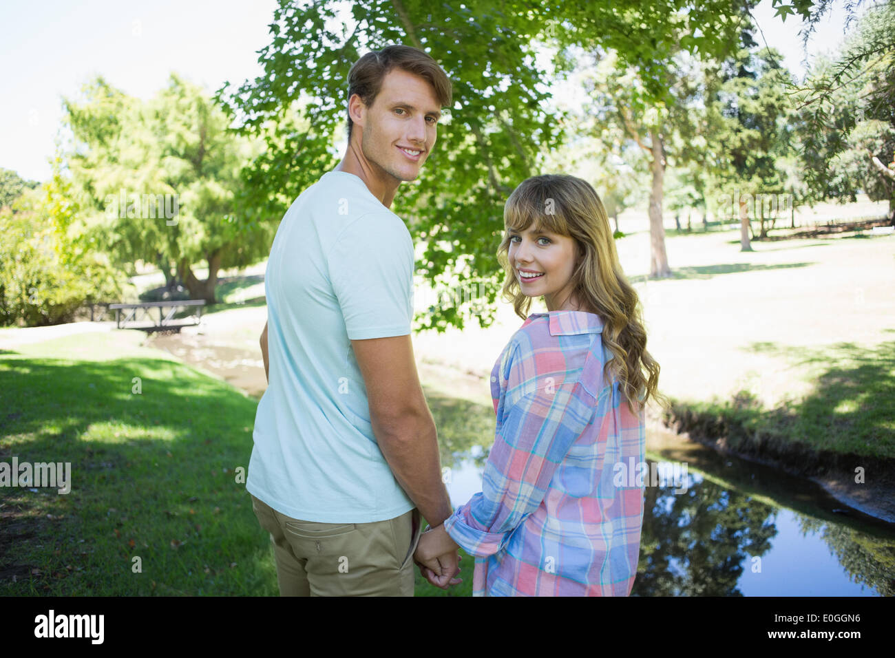 Cute Couple Walking Hand In Hand In The Park Smiling At Camera Stock