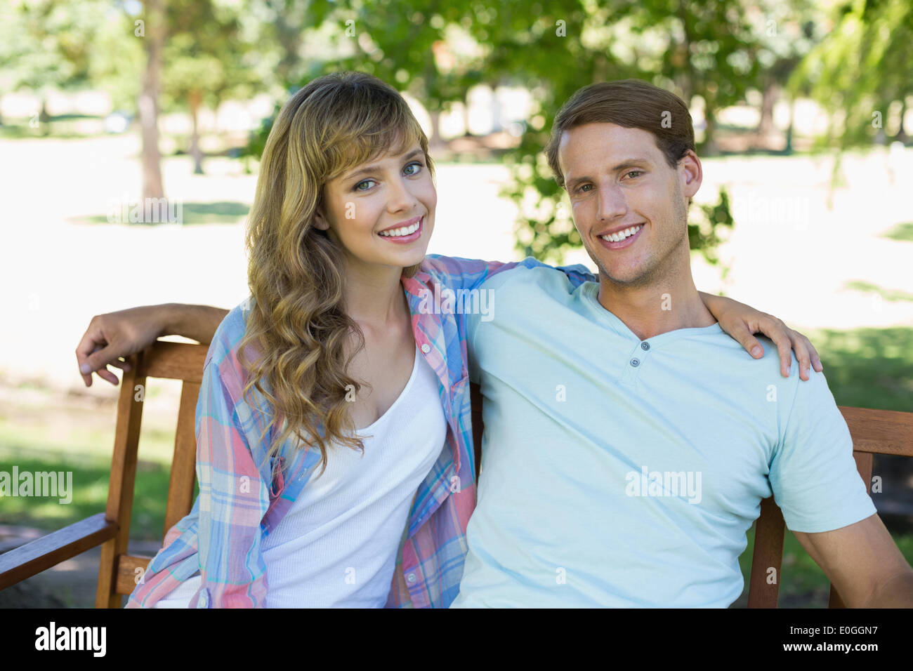 Cute couple sitting on bench in the park smiling at camera Stock Photo ...