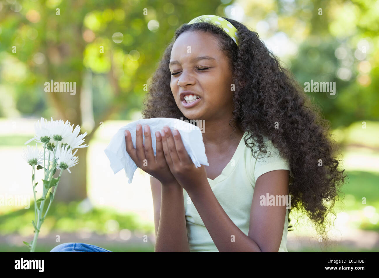 Young girl sitting by flower and sneezing in the park Stock Photo - Alamy
