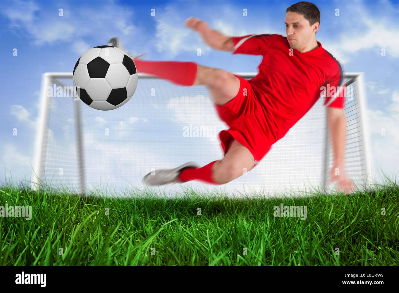 Fit football player jumping and kicking ball Stock Photo - Alamy