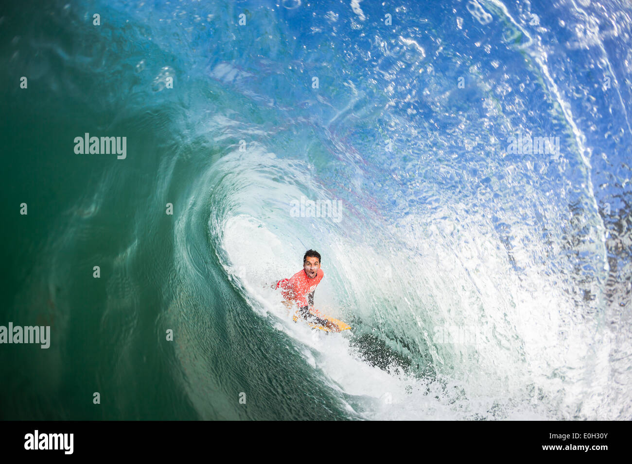 Surfing body-boarder rides hollow ocean blue wave tube, a swimming ...